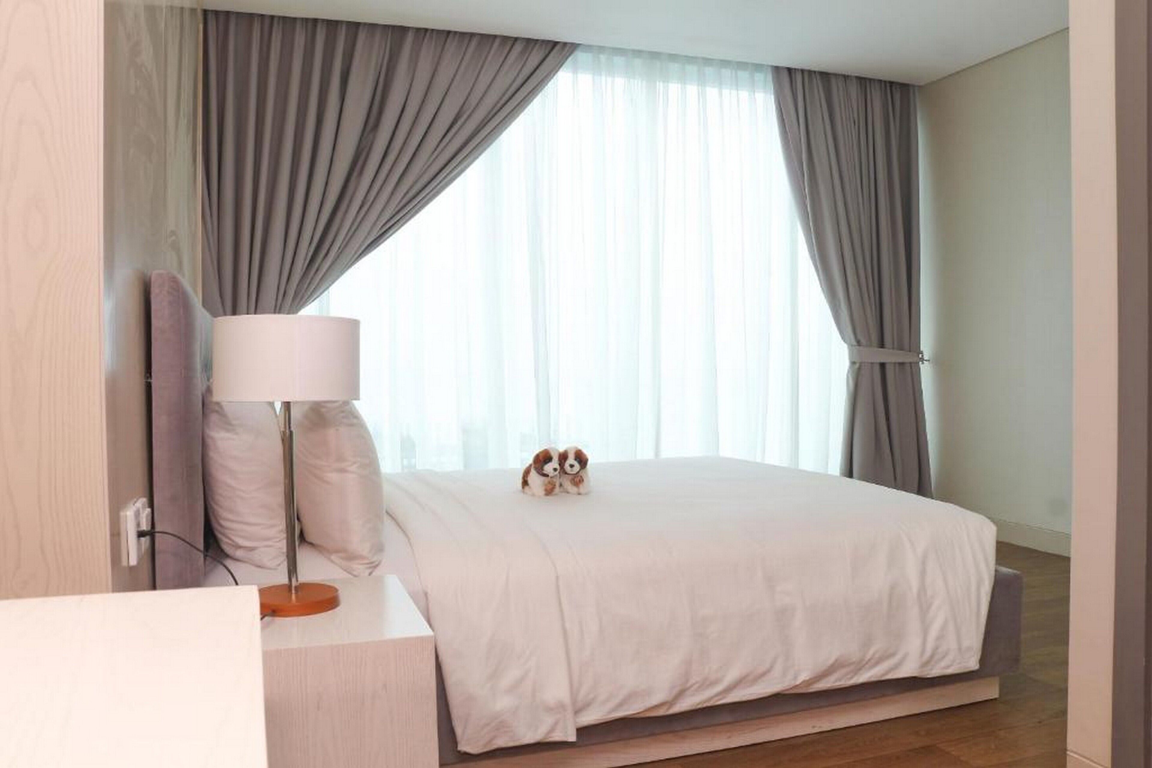 Quarto de hotel com cama, abajur e janela com cortinas.