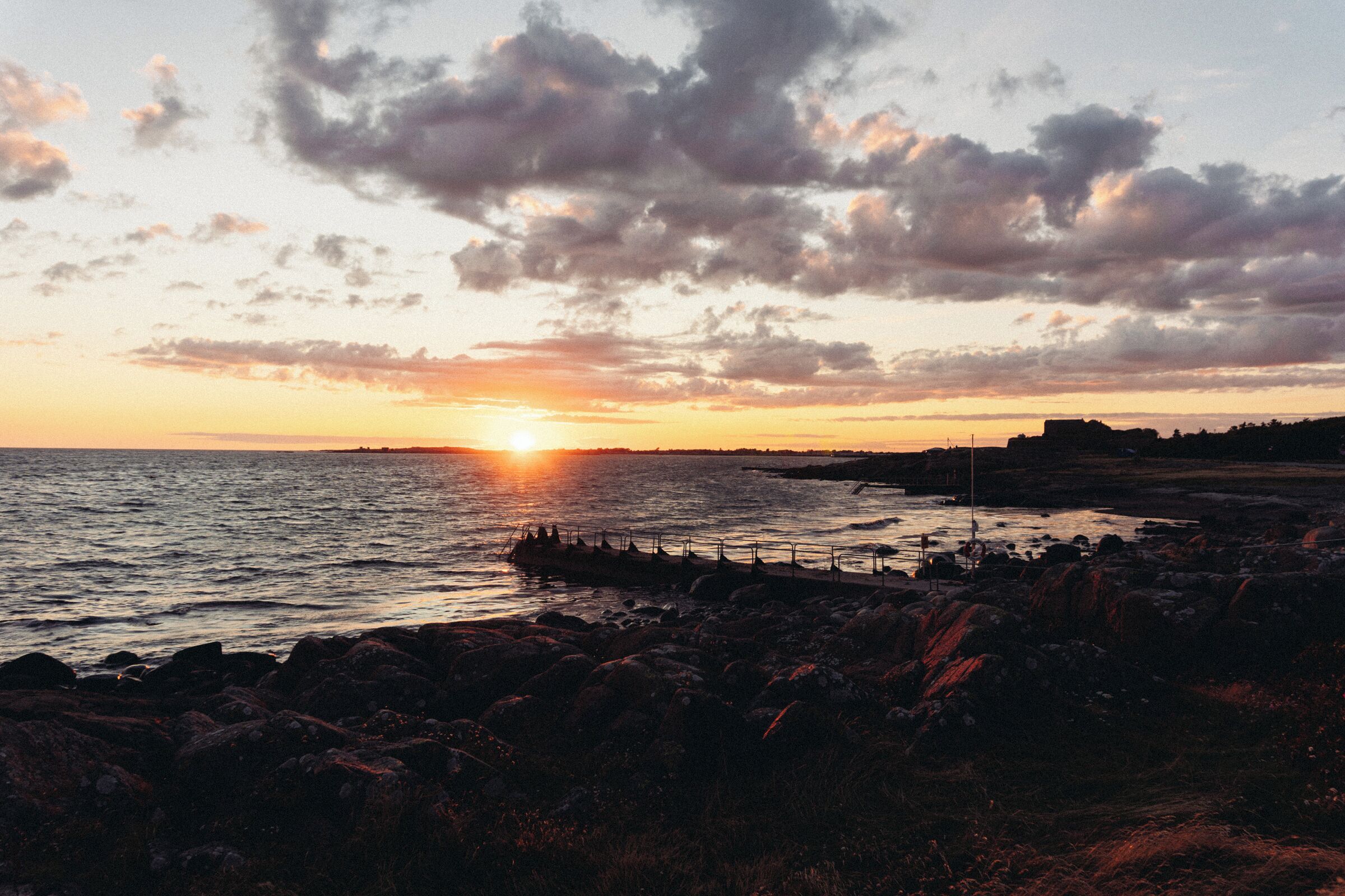 Um pôr do sol costeiro com uma linha de costa rochosa e um píer que se estende sobre a água.