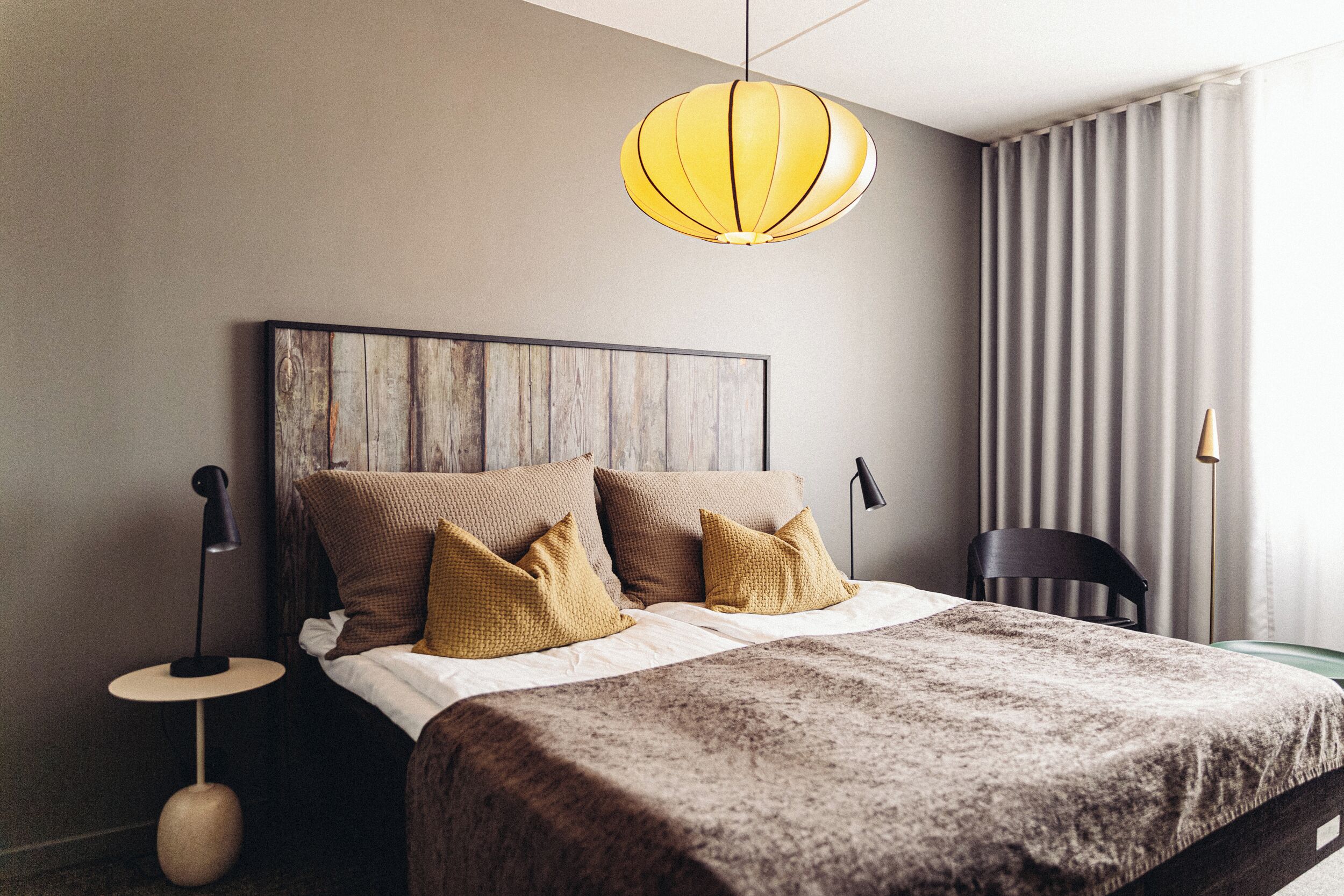 Cama bem arrumada com manta texturizada, cabeceira de madeira e duas luminárias laterais.