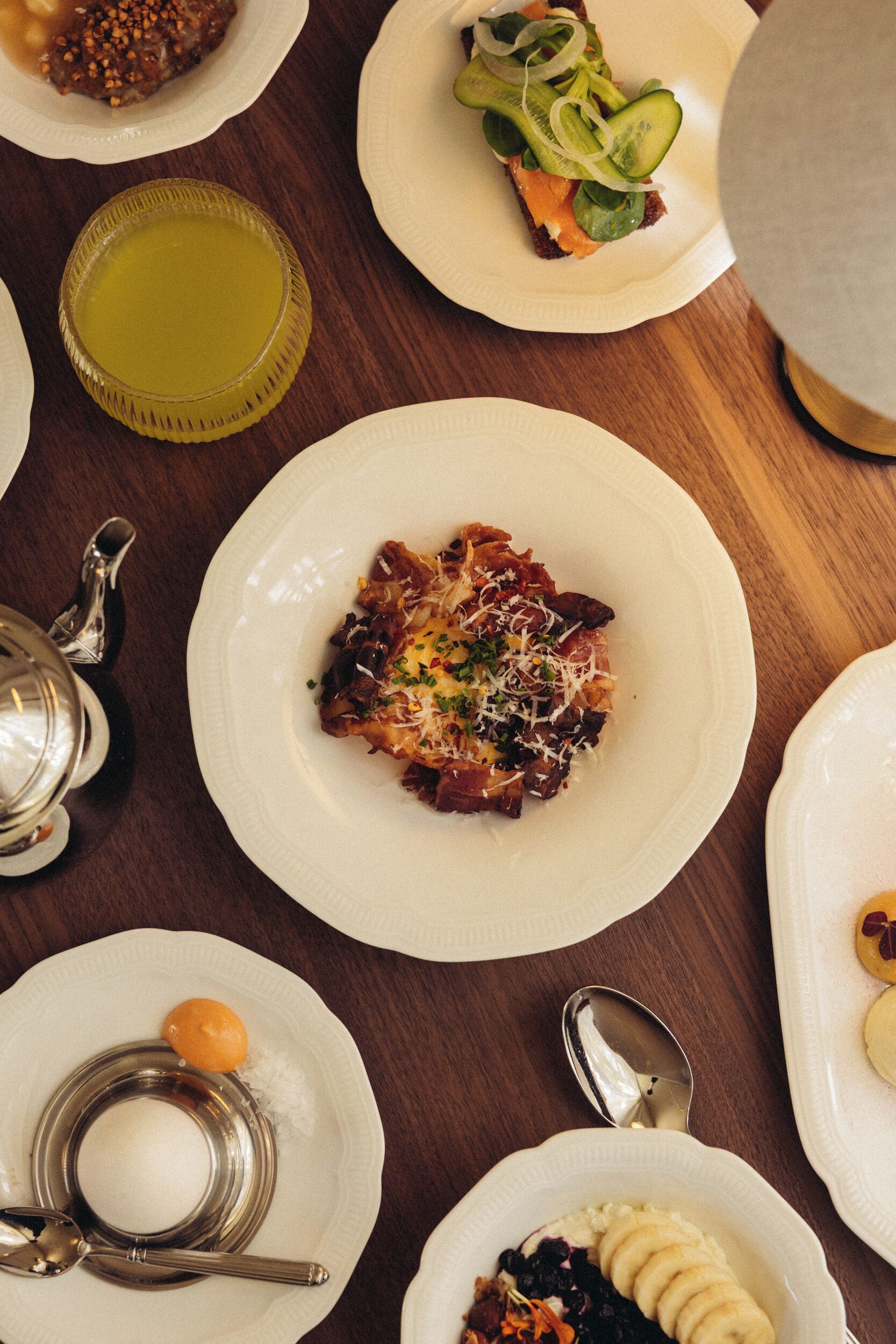 Uma mesa com diversos pratos e utensílios, incluindo pratos com comida, um copo de líquido amarelo e colheres de servir de metal.