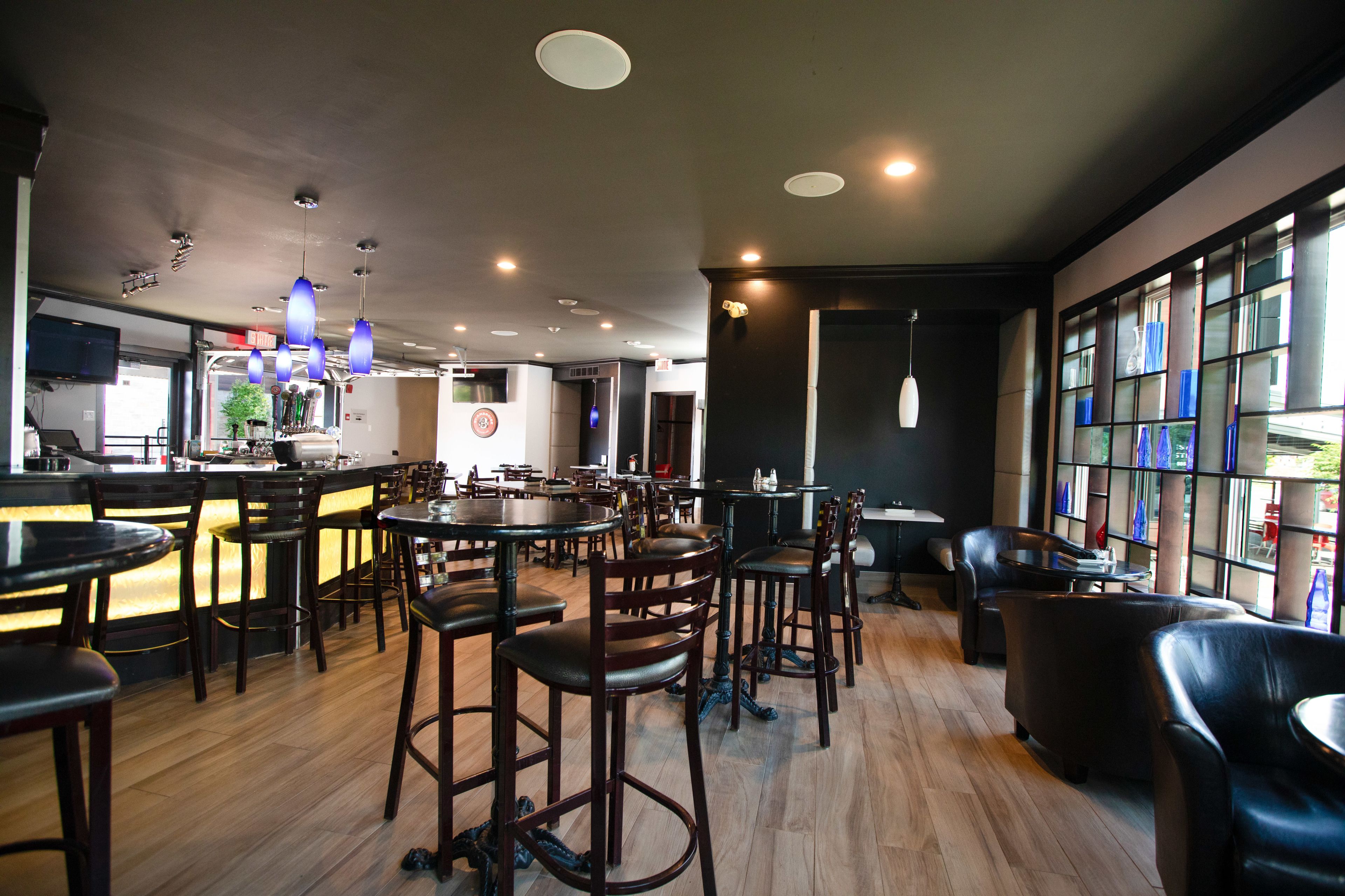 Um restaurante com piso de madeira, várias mesas e cadeiras, e um espaço de bar.