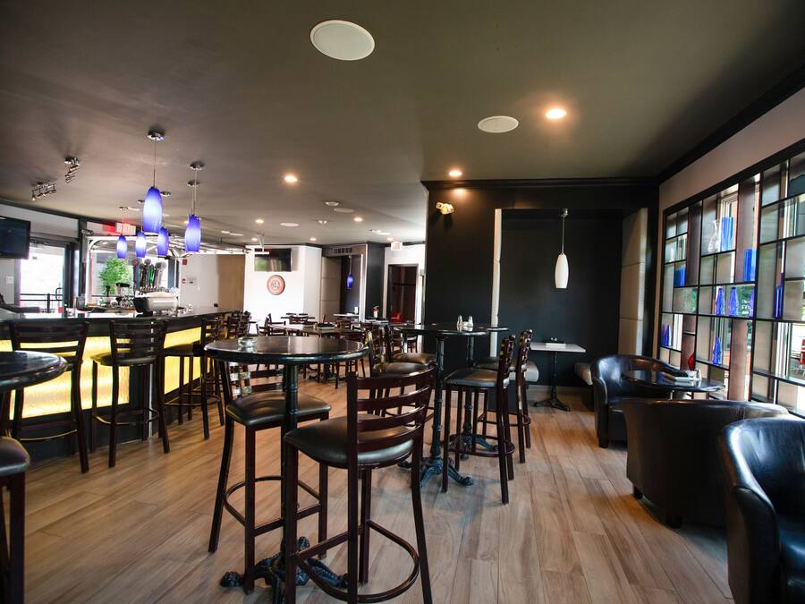 Um restaurante com piso de madeira, várias mesas e cadeiras, e um espaço de bar.