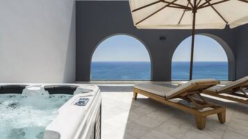 Uma banheira de hidromassagem com painel de controle, duas cadeiras de descanso e um guarda-sol numa varanda com vista para o oceano.