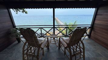 Uma área de estar coberta ao ar livre, com duas cadeiras de vime e uma pequena mesa, com vista para o mar.