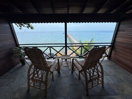 Uma área de estar coberta ao ar livre, com duas cadeiras de vime e uma pequena mesa, com vista para o mar.
