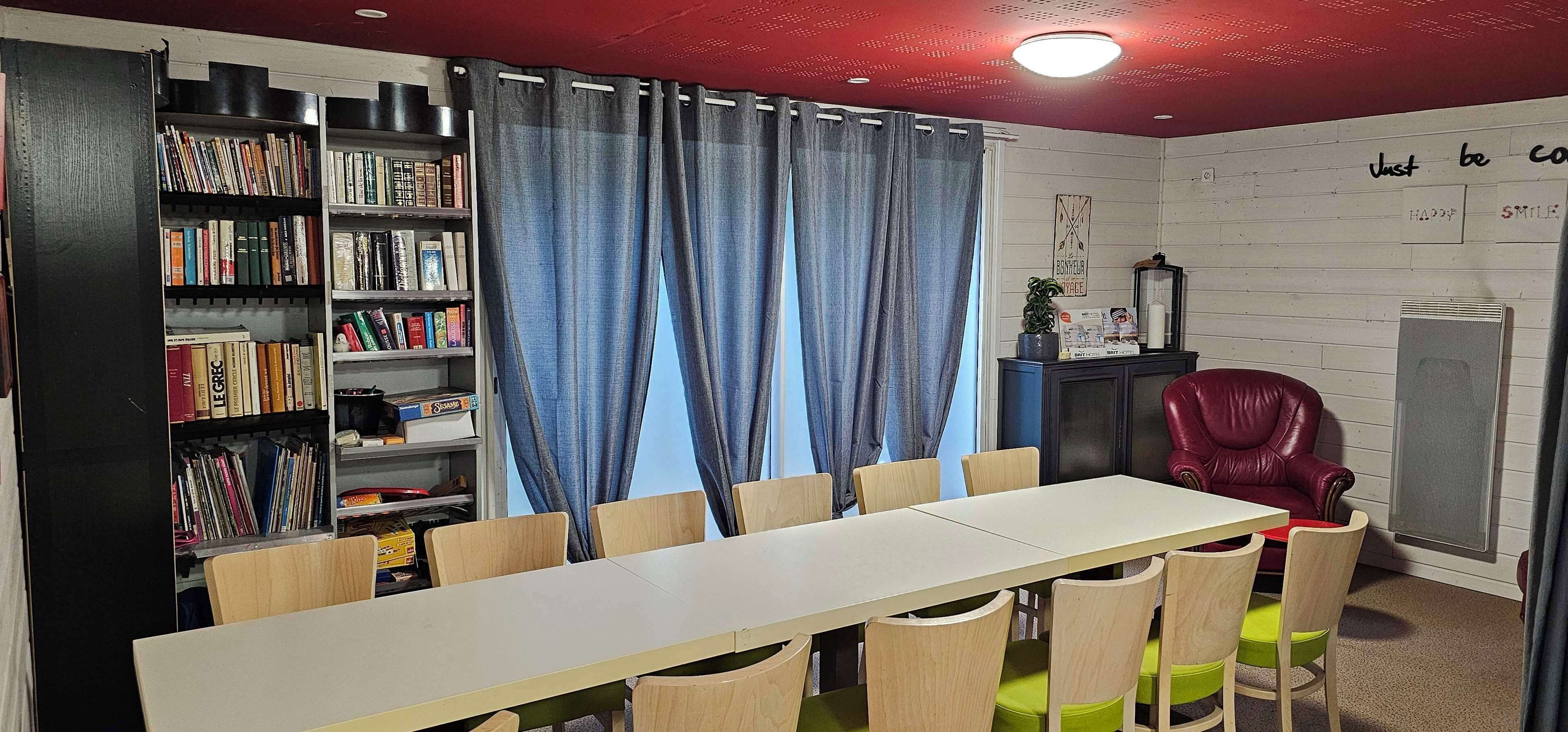 Um quarto com uma mesa comprida, cadeiras, uma estante de livros, uma poltrona de couro vermelho e uma parede com frases motivacionais.