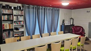Um quarto com uma mesa comprida, cadeiras, uma estante de livros, uma poltrona de couro vermelho e uma parede com frases motivacionais.