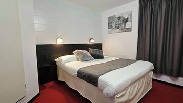 Cama bem arrumada com edredom branco e cinza, dois travesseiros e um cobertor cinza. Duas luminárias fixadas na parede estão sobre a cama.