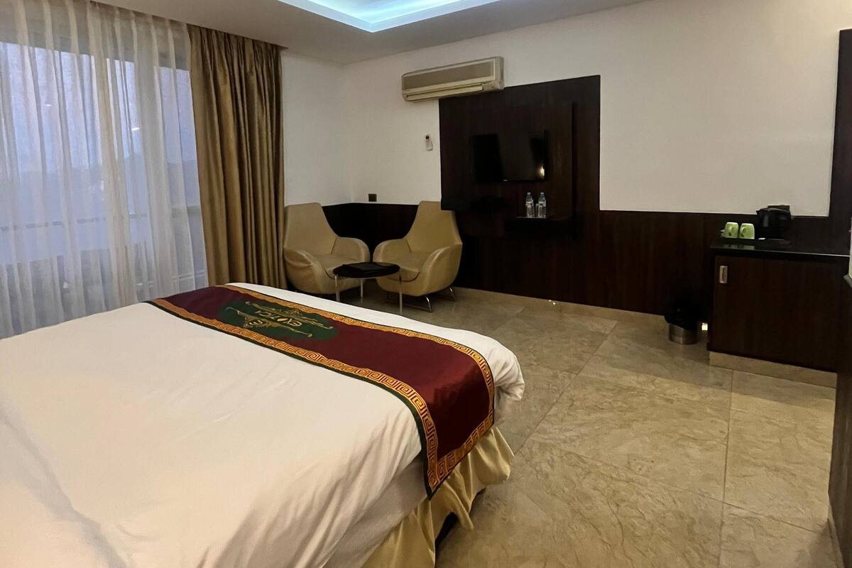 Quarto de hotel com uma cama, uma escrivaninha, uma cadeira, um ventilador de teto, ar condicionado e uma TV.