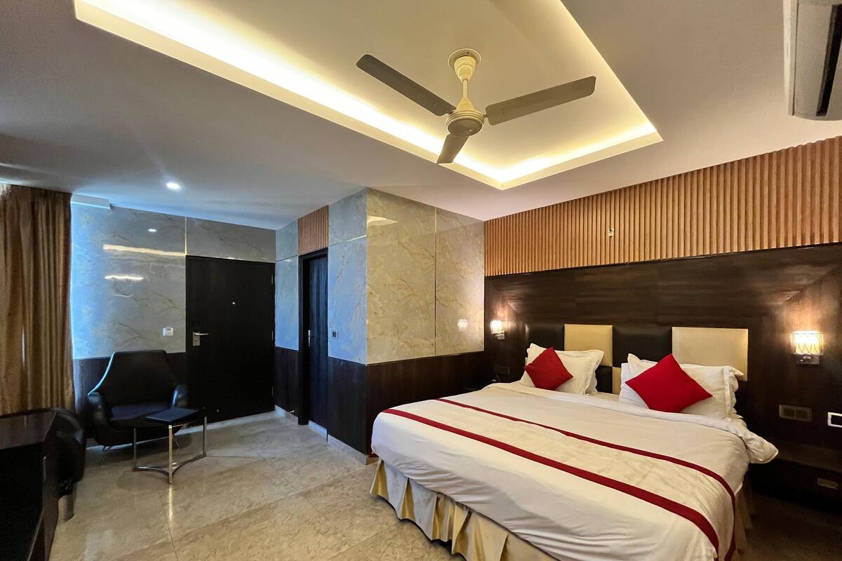 Quarto de hotel moderno com uma cama grande, um ventilador de teto e uma área de estar com uma poltrona.