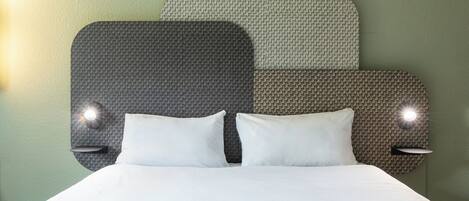 Uma cama com cabeceira, duas mesas de cabeceira e uma luminária fixada na parede.