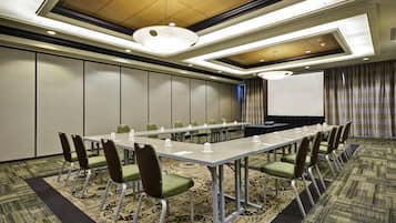 Uma sala de conferências com uma mesa comprida, cadeiras e uma tela de projeção.