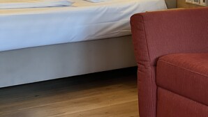 Quarto de hotel com uma cama grande, duas luminárias de cabeceira e uma poltrona vermelha.