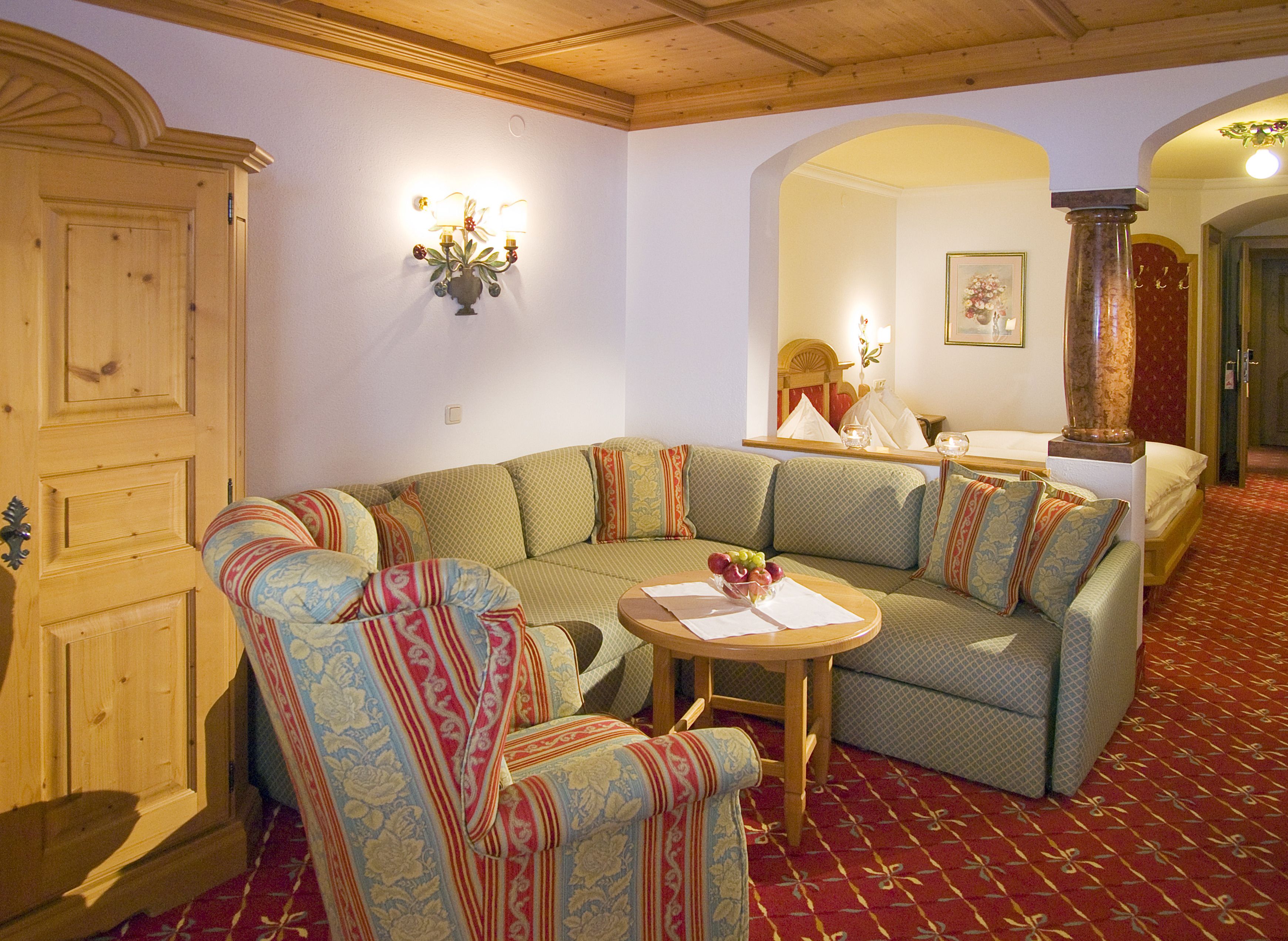 Um quarto aconchegante com um sofá verde grande, um armário de madeira e uma pequena mesa com um vaso de flores.