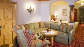 Um quarto aconchegante com um sofá verde grande, um armário de madeira e uma pequena mesa com um vaso de flores.