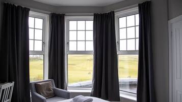 Quarto de hotel com uma grande janela, uma cama, uma cadeira e vista para um campo de golfe.