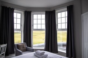 Quarto de hotel com uma grande janela, uma cama, uma cadeira e vista para um campo de golfe.