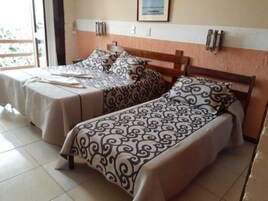 Quarto com duas camas, cada uma com roupa de cama estampada, cabeceira de madeira e uma janela com vista.