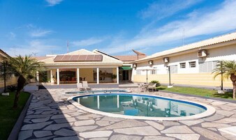 Uma piscina com um caminho de pedra, um alpendre coberto e um edifício com telhado de azulejos.