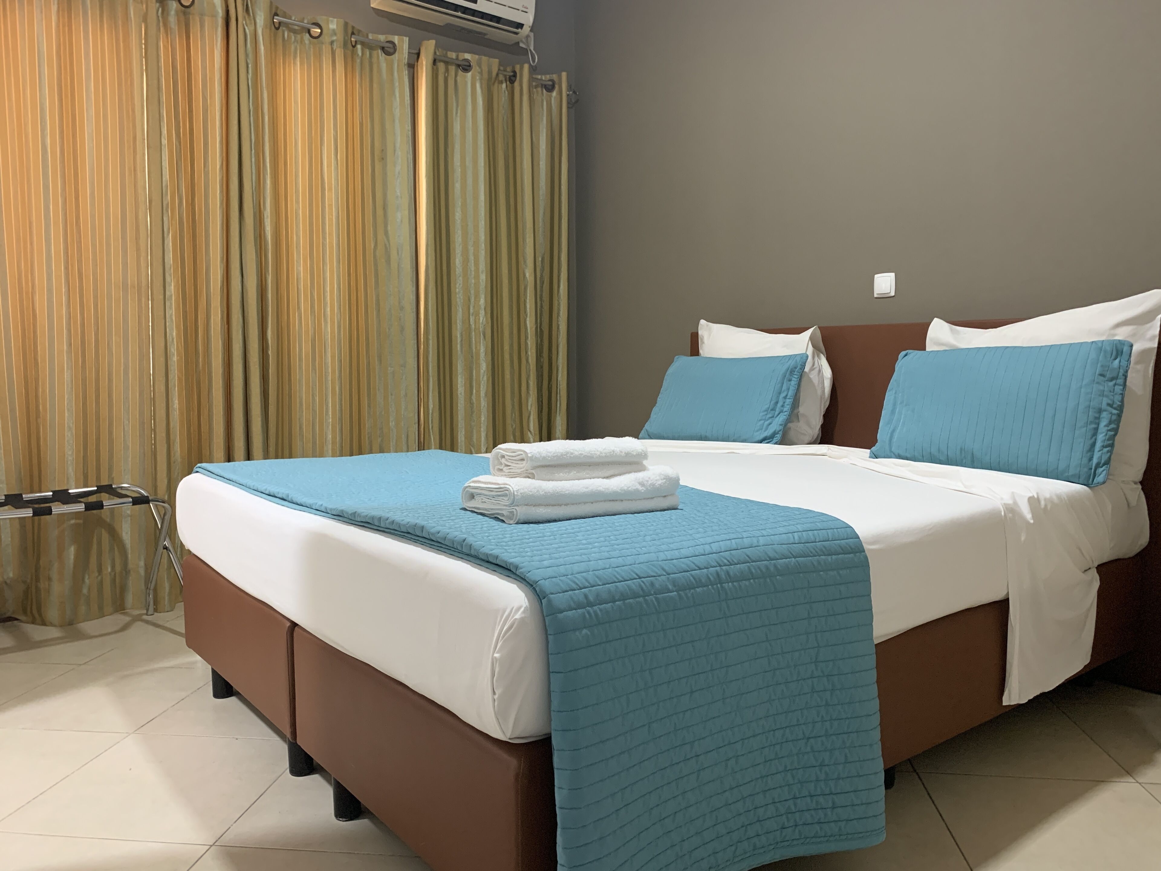 Cama bem arrumada com roupa de cama azul, cabeceira marrom e manta azul.
