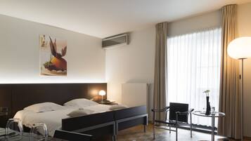 Quarto de hotel moderno com cama, mesa de cabeceira, luminária, cadeira e uma pequena mesa com um vaso.