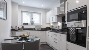 Cozinha moderna com armários brancos, forno Bosch e área de refeições com mesa de vidro e duas cadeiras.
