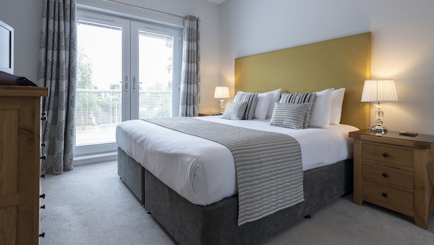 Quarto moderno com cama grande, abajures e vista pela janela com cortinas.