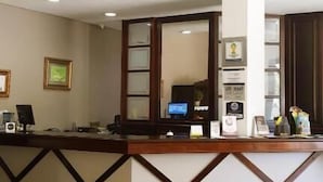 Uma área de recepção com balcão de madeira, computador, quadros nas paredes e um espelho.