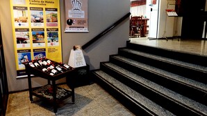 Um saguão de hotel com uma escadaria, um quadro de avisos com anúncios do hotel e uma exposição de vinhos.
