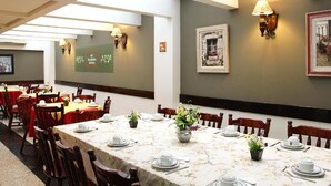Uma sala de jantar com mesas preparadas para o serviço, um letreiro verde na parede e luminárias fixadas na parede.