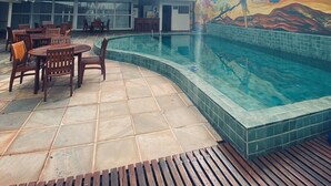 Uma área de piscina no terraço com um mural, edifícios altos e um espaço de estar coberto.