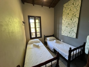 Quarto pequeno e limpo com duas camas individuais, uma janela e uma obra de arte na parede.