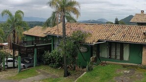 Uma casa tradicional com telhado em telhas, fachada verde e pequena varanda.