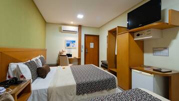 Quarto de hotel com duas camas, uma escrivaninha, televisão e ar condicionado.