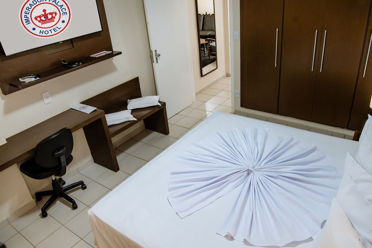 Quarto de hotel com cama, escrivaninha, cadeira, guarda-roupa e espelho.