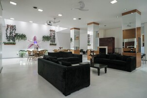 Um lobby moderno com sofás pretos, uma mesa de centro e uma área de refeições com cadeiras de vime.