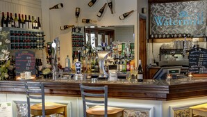 Uma área de bar com balcão de madeira, banquetas e diversos tipos de garrafas e copos.