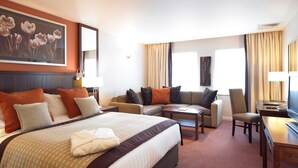 Quarto de hotel com uma cama grande, um sofá, uma escrivaninha e uma televisão.