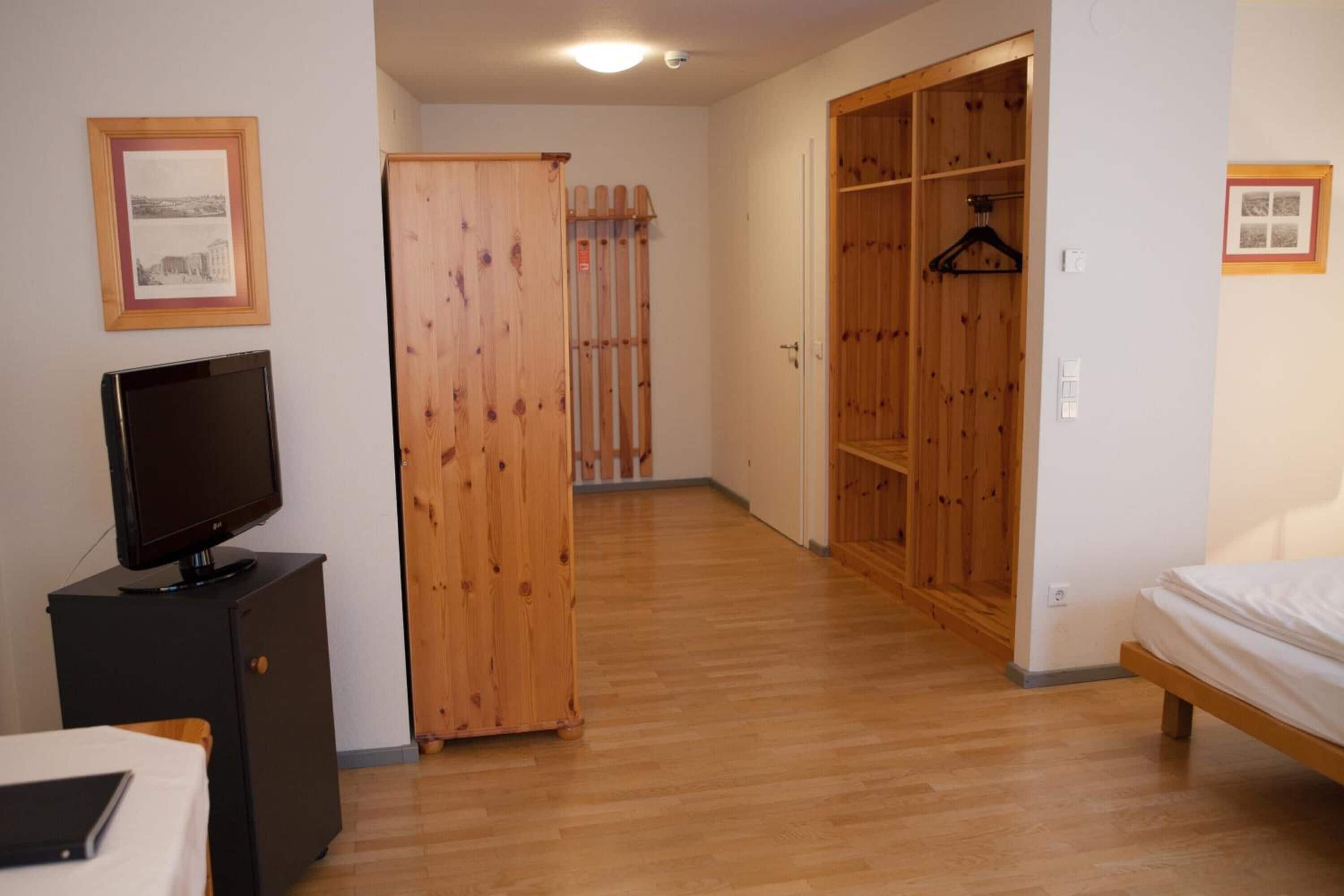 Quarto com uma cama, uma TV sobre um móvel, um guarda-roupa de madeira e um quadro na parede.