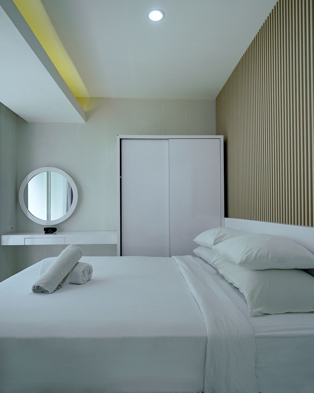Quarto de hotel moderno com cama, um espelho redondo, guarda-roupa e luminária fixada na parede.