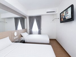 Quarto de hotel com duas camas, um espelho grande, ar condicionado e uma tela de televisão exibindo um anúncio.