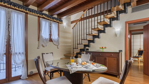 Uma área de jantar com uma mesa redonda, cadeiras, uma escada e vista para o exterior.
