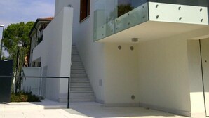 Um edifício moderno de vários andares com varanda de vidro, escadaria e telhado plano.