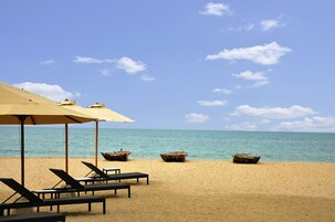 Uma praia com cadeiras de sol e um grande guarda-sol, barcos na água e um céu limpo.