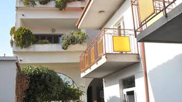 Um edifício de vários andares com varandas, uma escadaria e uma pequena área ajardinada.