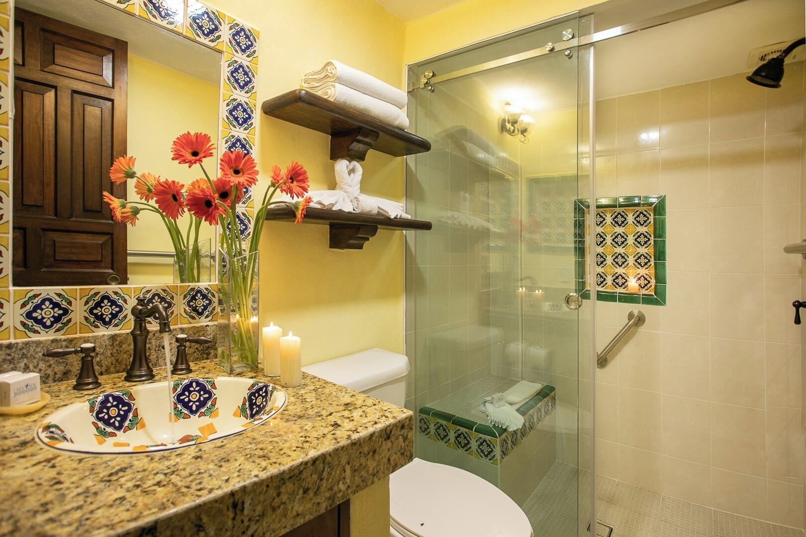 Casa de banho com bancada de granito, pia com cuba decorativa, espelho, cabine de chuveiro em vidro e porta-toalhas.