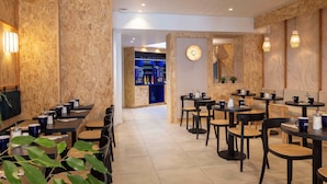 Restaurante moderno com paredes de madeira, várias mesas com cadeiras e um balcão de bebidas azul ao fundo.