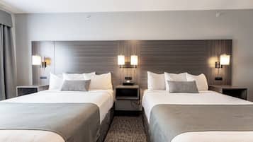 Quarto de hotel com duas camas, mesa de cabeceira com abajur e luminária na parede.