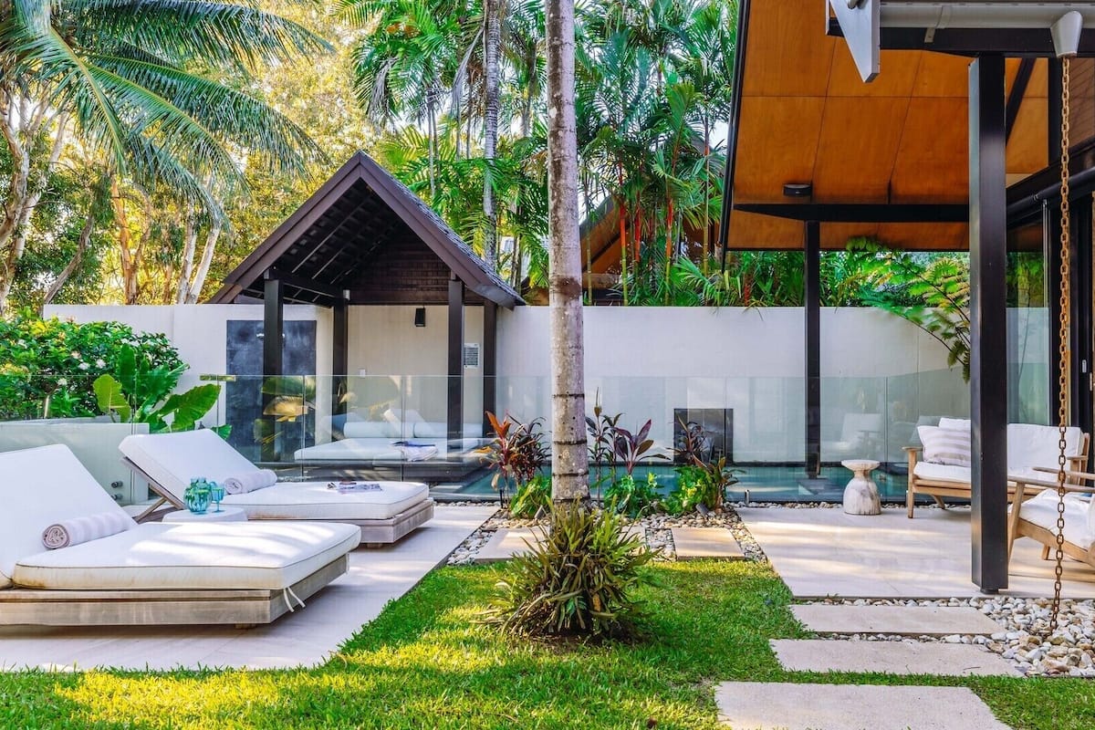 Uma área de lounge moderna ao ar livre, com espreguiçadeiras, uma piscina pequena e vegetação tropical exuberante.