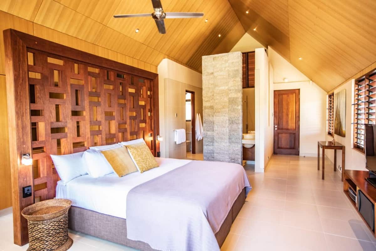 Um quarto espaçoso com uma cama grande, cabeceira de madeira e um ventilador de teto.